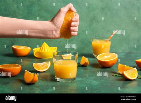 Female hand squeezing orange juice into glass on green background Stock Photo - Alamy