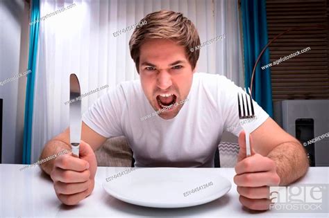 Angry Man Holding Knife And Fork With Empty Plate On Table Stock Photo