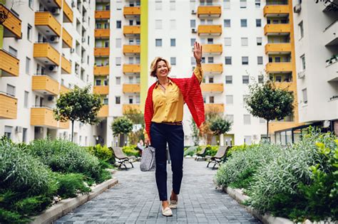 공원에서 걷는 짧은 금발 머리와 화려한 백인 유행 시니어 여성의 전체 길이 친구에게 손을 흔들고 지갑을 들고 가득 찬에 대한
