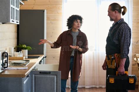 Young Worried Housewife Looking At Plumber And Explaining Him Problem