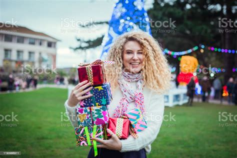 손에 화려한 선물 상자의 타워와 행복 금발 곱슬 여자 미소 배경에 밝게 크리스타마스 나무와 장식 된 공원에서 야외 에서 시간을 즐기고 축제 새해 분위기입니다 공간을