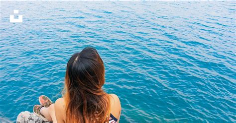 흰색과 파란색 줄무늬 탱크 탑을 입은 여자는 수역 근처의 바위에 앉아 있습니다 사진 Unsplash의 무료 소녀 이미지