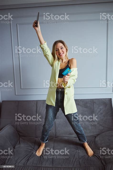 스마트폰을 들어 올리는 동안 신용 카드를 보여주는 기뻐하는 여성 신용 카드에 대한 스톡 사진 및 기타 이미지 신용 카드 점프 여자 Istock