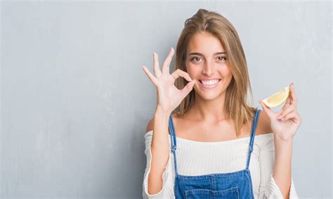 그런 지 위에 아름 다운 젊은 여자 회색 벽 잡고 손가락으로 우수한 기호 확인 서명 하 고 레몬 슬라이스 개념에 대한 스톡 사진