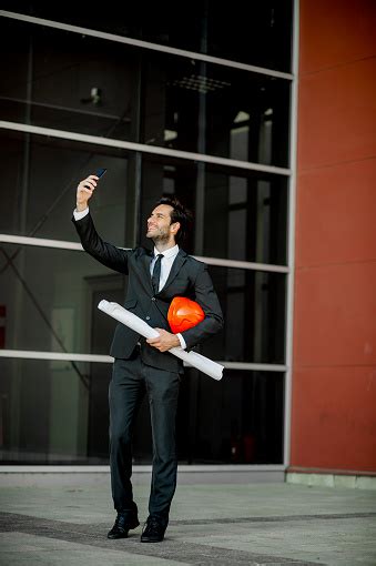 전화를 사용하여 프로젝트와 하드 모자를 가진 젊은 건설 엔지니어 남자 건물 외관에 대한 스톡 사진 및 기타 이미지 건물 외관 건설 산업 건설 현장 Istock