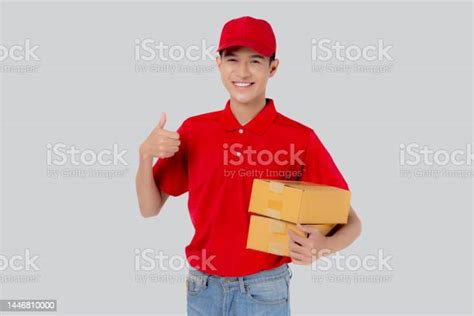 유니폼 빨간색과 모자를 쓴 젊은 아시아 남자는 상자 스택을 들고 서 있고 엄지손가락을 들고 고립된 흰색 배경 직원은 화물 택배 및 배달 운송 및 서비스 물류 및 화물을 들고