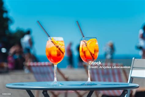 오렌지 스프리츠 아페롤 음료 두 잔은 바다와 나무가 흐릿한 사람들의 배경을 볼 수 있는 야외 테이블에 칵테일을 마신다 여름 저녁 칵테일에 대한 스톡 사진 및 기타 이미지