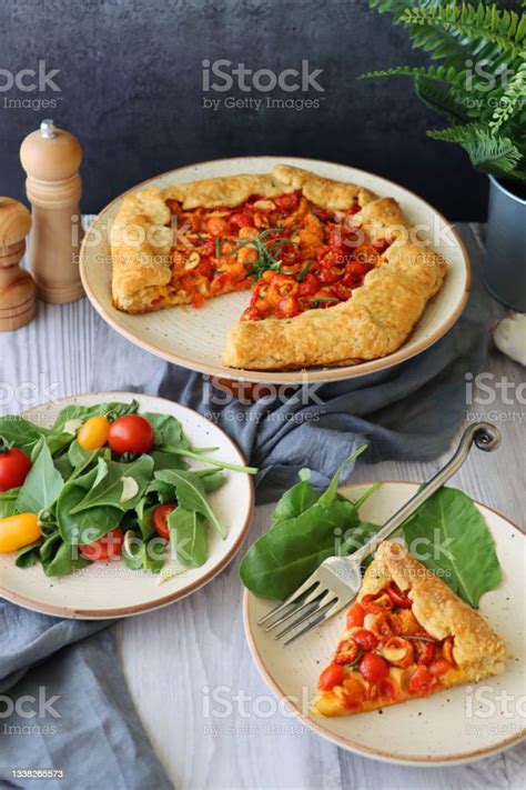 포크와 사이드 샐러드와 흰색 접시에 집에서 만든 짭짤한 갈레트 레시피의 조각의 이미지 케이크 스탠드에 소박한 파이 옆에 페스토