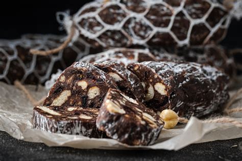 검은 배경에 아몬드 헤이즐넛 건포도로 채워진 초콜릿 살라미 가루 설탕을 뿌린 이탈리아 달콤한 소시지 모양의 디저트 크리스마스와 새해 축제 과자 갈색에 대한 스톡 사진 및