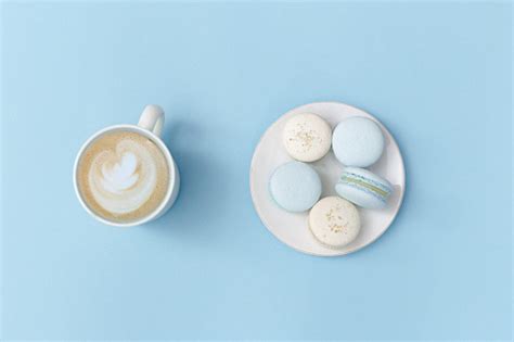 밝은 파란색 배경에 맛있는 마카롱과 큰 찻잔과 흰색 접시에 Coffe 카푸치노 아트 폼 달콤한 음식 개념입니다 맨 위 보기 플랫