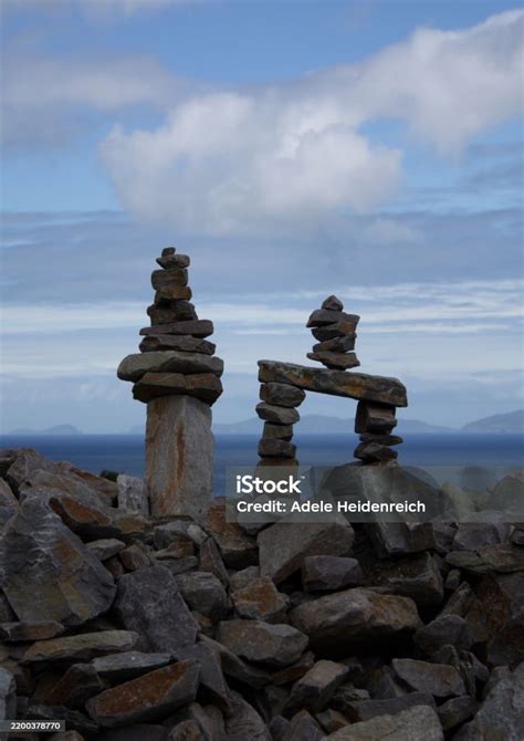 섬세하게 균형 잡힌 돌 돌탑은 아일랜드의 흰 구름으로 가득 찬 하늘 아래 깊고 푸른 바다와 먼 섬과 함께 험준한 해안을 배경으로 서 있습니다 0명에 대한 스톡 사진 및 기타