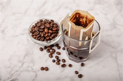 집에서 커피를 만드는 추세 갈색 배경에 커피 원두가 든 유리잔에 신선한 음료가 담긴 가방을 드립한다 컵에 양조하기위한 분쇄 커피 용지 필터를 사용하여 커피를 드립합니다