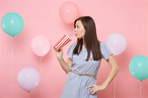 블루 입고 예쁜 여자의 초상화 화려한 공기 풍선 파스텔 핑크 배경에 플라스틱 컵에서 찾고 따로 마시는 콜라 나 소 다를 드레스