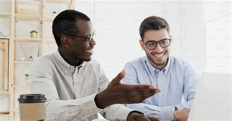 팀웍 개념입니다 노트북을 함께 사용하는 다양한 미소 짓는 현대 사업가들 백인 사무실에서 백인 동료에게 손으로 노트북 화면에 무언가를 보여주는 아프리카 동료 사진