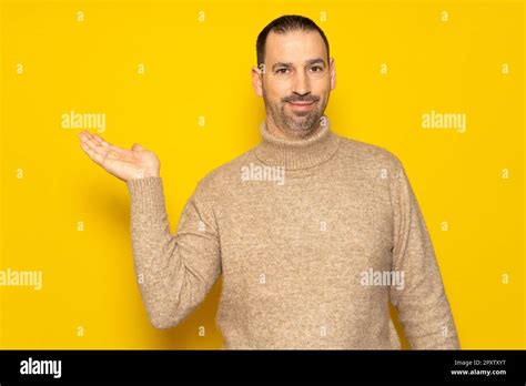 Bearded Hispanic Man In His 40s Wearing A Beige Turtleneck Presenting