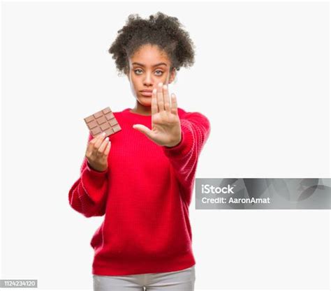 젊은 아프리카 미국 여자와 격리 된 배경 위에 초콜릿을 먹고 열 심각 하 고 자신감 표현 방어 제스처 정지 표시를 하 고 손을
