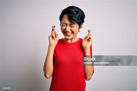 고립 된 흰색 배경 제스처 손가락 위에 서 캐주얼 빨간 티셔츠를 입고 젊은 아름다운 아시아 소녀는 희망과 눈을 감고 미소 교차 행운과 미신 개념 T 셔츠에 대한 스톡 사진