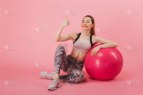 快乐的女运动员坐在地板上拿着健身球