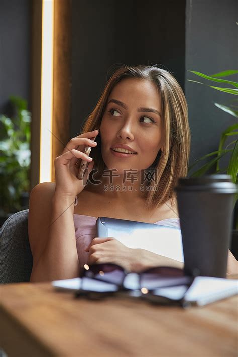 年轻的亚洲漂亮女人坐在咖啡店的桌子旁用智能手机打电话高清摄影大图 千库网