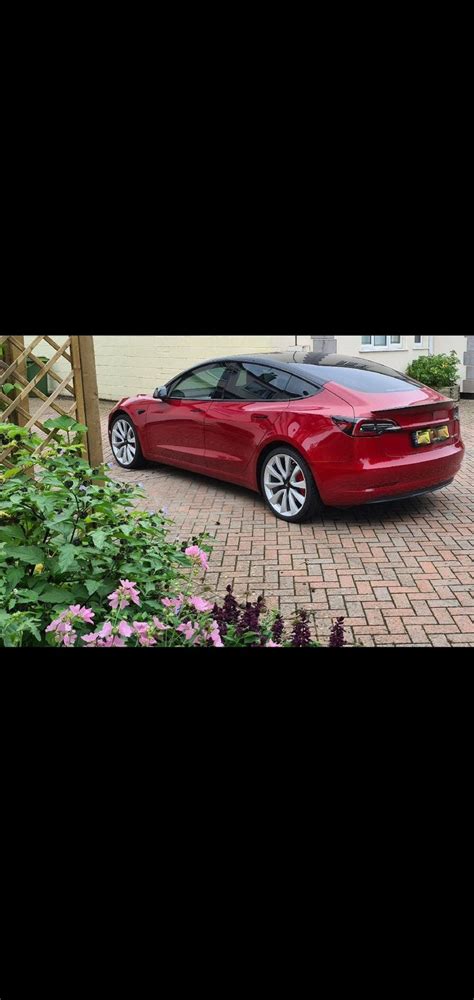 A Red Sports Car Parked In Front Of A House Next To Some Purple Flowers And Bushes