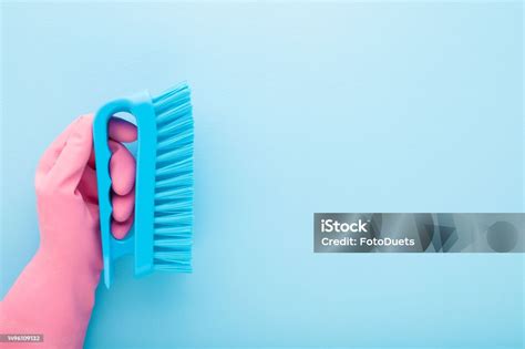 분홍색 고무 보호 장갑을 끼고 밝은 파란색 테이블 배경에 새 청소 브러시를 보여주는 깨끗한 손 파스텔 색상 근접 촬영 텍스트를