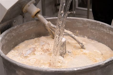 빵집의 반죽 기계에 물을 붓고 빵 반죽을 반죽하는 과정을 클로즈업합니다 반죽 반죽을위한 산업용 믹서 빵 반죽을 만드는 단계 중