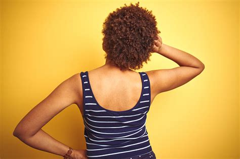 여름 티셔츠를 입은 아프리카 계 미국인 여성이 고립된 노란색 배경 에 머리를 손으로 의심을 생각하고 뒤로 T 셔츠에 대한 스톡