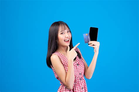 파란 배경에 고립 된 휴대 전화를 들고있는 동안 초상화 아시아 행복 어린 소녀 쾌활하고 플라스틱 신용 카드를 보여주는 아시아에