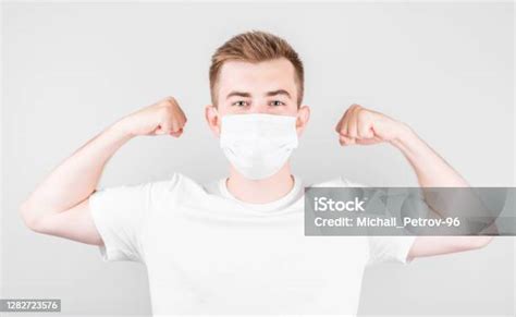 팔을 들어 올려 서 있는 의료용 보호 마스크를 착용한 잘생긴 미국 남자의 초상화는 강한 이두근을 보여줍니다 격리된 배경입니다 20 24세에 대한 스톡 사진 및 기타 이미지