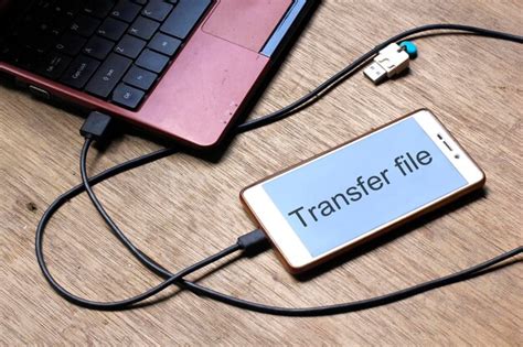 Premium Photo Mobile Phone Connected To Laptop Through Usb Cable On Table
