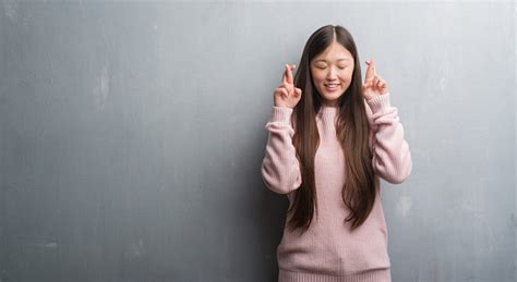 회색 벽 횡단 손가락 희망 및 눈을 감고 미소를 통해 젊은 중국 여자 행운과 미신의 개념입니다 겨울에 대한 스톡 사진 및 기타
