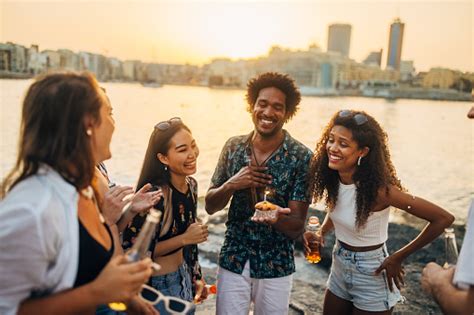 흑인 남성이 생일 케이크를 손에 들고 다양한 가장 친한 친구들에게 둘러싸인 해변에 서서 생일 소원을 빌고 있습니다 25 29세에 대한 스톡 사진 및 기타 이미지 Istock