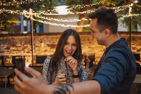 아름다운 커플남자와 여자는 쾌활한 분위기와 상쾌한 칵테일로 둘러싸인 오픈 테라스의 카페에서 여름 데이트를 즐깁니다 그들의 얼굴