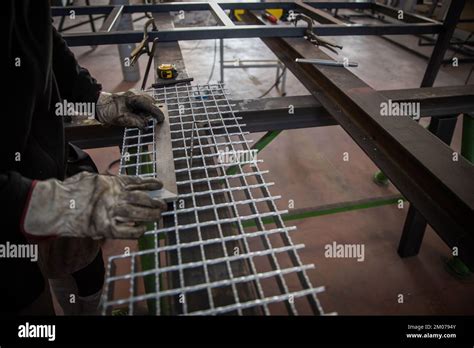 A Worker Takes Measurements Of A Grid With A Ruler On The Construction