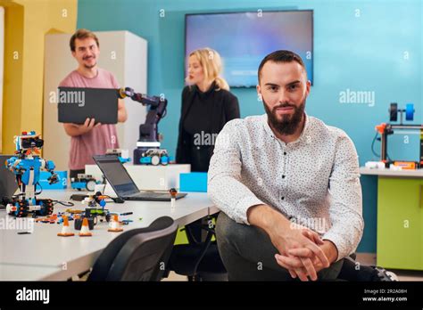 A Man Sitting In A Robotics Laboratory While His Colleagues In The