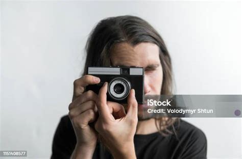 긴 머리와 흰색 배경에 빈티지 구식 필름 카메라를 들고 검은 셔츠에 카메라 뷰파인더를 보고 잘생긴 젊은 수염 남자 검은색에 대한