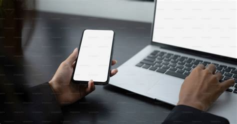 스마트폰을 들고 사무실 책상에서 컴퓨터 노트북으로 작업하는 사업가의 어깨 너머로 클로즈업 사진 Unsplash의 사진술 이미지