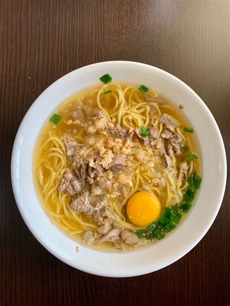 A White Bowl Filled With Noodles And Meat Next To An Egg On Top Of A