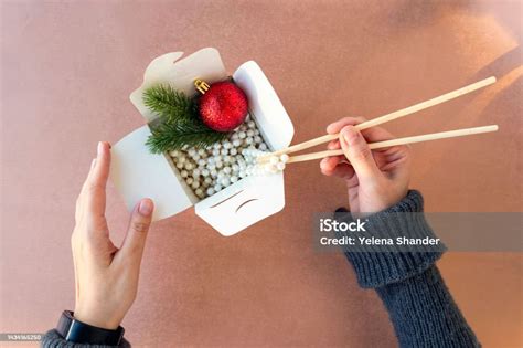 여성 손의 윗모습은 중국 젓가락이있는 음식 상자에서 흰색 구슬을 꺼냅니다 빨간 크리스마스 공 가지 및 크리스마스 구슬을 음식