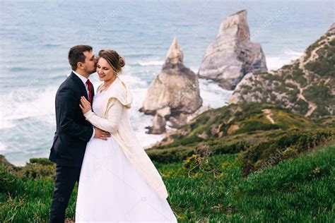 el novio abraza y besa a la novia en la costa del océano con vistas a t