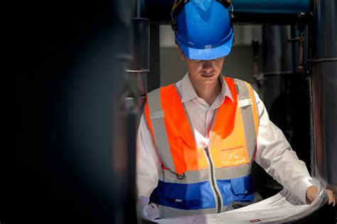 눈에 잘 띄는 장비를 착용하고 파란색 헬멧을 쓴 산업 노동자가 복잡한 기계 네트워크를 꼼꼼하게 살핍니다 엔지니어는 운영 효율성과 안전성을 유지하기 위해 최선을 다하고