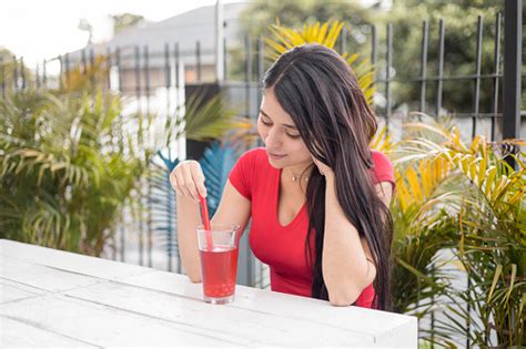 Woman Enjoying A Drink In A Garden In The Daytime She Wears A Red Dress