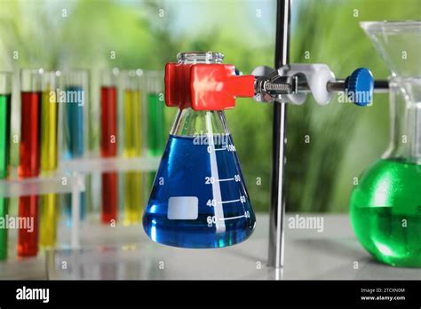 Retort Stand And Laboratory Flask With Liquid On Table Against Blurred Background Closeup Stock