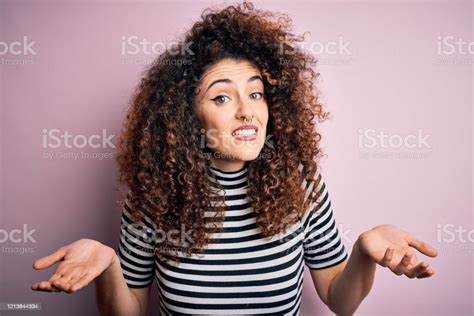 곱슬 머리와 피어싱 캐주얼 줄무늬 티셔츠를 입고 젊은 아름다운 여성은 팔과 손을 들고 단서와 혼란 표정을 의심 개념 T 셔츠에
