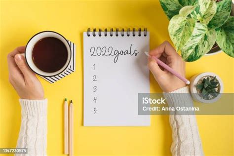 데스크톱 빈 메모장과 여자 손 쓰기 2022 계획 및 목표 텍스트 차와 식물 한 잔노란색 작업 테이블 배경의 평평한 평지 상단 보기 모의 2022년에 대한 스톡 사진 및