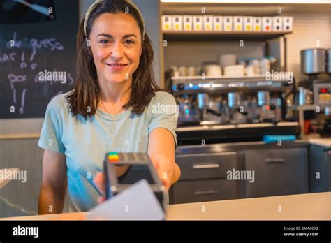 A Brunette Caucasian Waitress Smiling Handing Over The Dataphone To