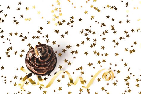 초콜릿 아이싱초콜릿 컵케이크 골드 스파클 불타는 촛불을 흰색 배경에 황금별 모양의 색종이와 파티 스트리머로 장식합니다 플랫 레이 스타일 디자인에 대한 모형 공간을 복사합니다