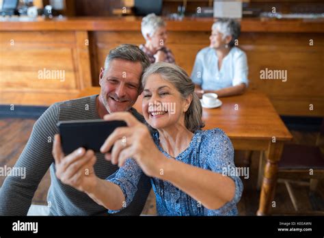 Smiling Senior Couple Taking Selfie With Mobile Phone In Restaurant