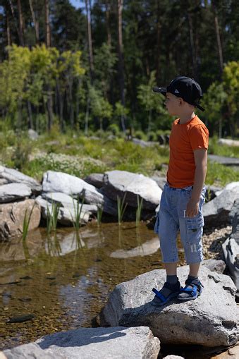 여름에는 소년이 산 강 근처의 바위 위에 서 있습니다 한 아이가 돌이 흩어져 있는 작고 아름다운 산의 강둑을 따라 여행합니다 산 강을 여행하는 개념입니다 강에 대한 스톡