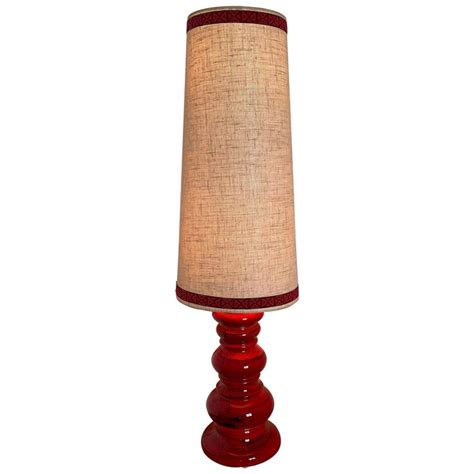A Red Table Lamp With A Beige Shade On The Top And A White Background